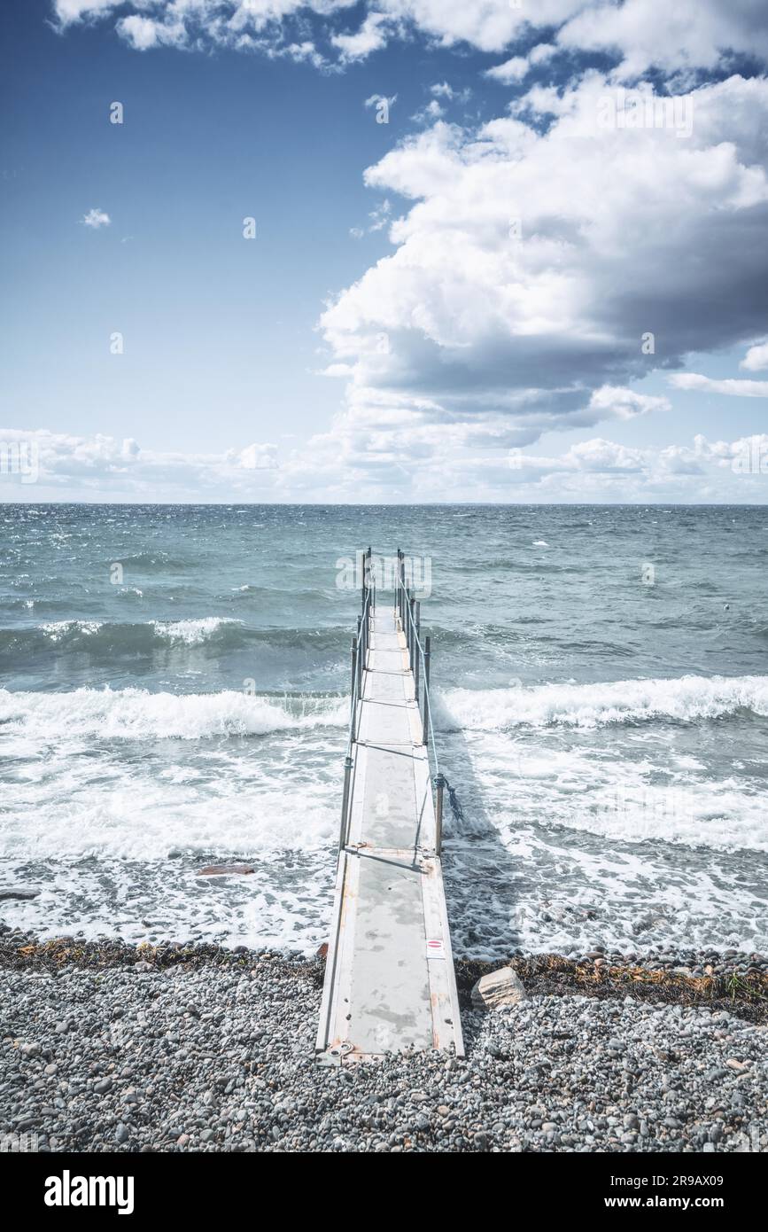 Small pier at a cold sea with waves coming in on the pebble beach Stock ...