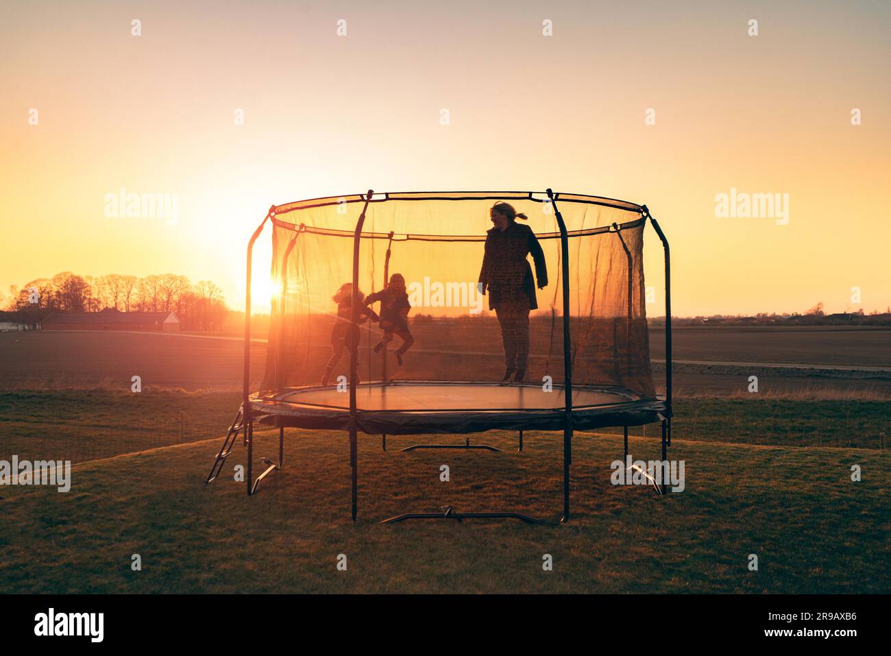 Trampoline on a lawn in the sunset with two kids and a young woman ...