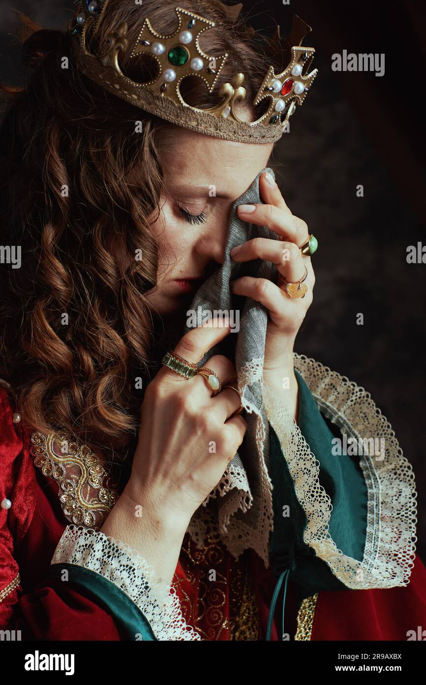 sad medieval queen in red dress with handkerchief and crown crying on ...