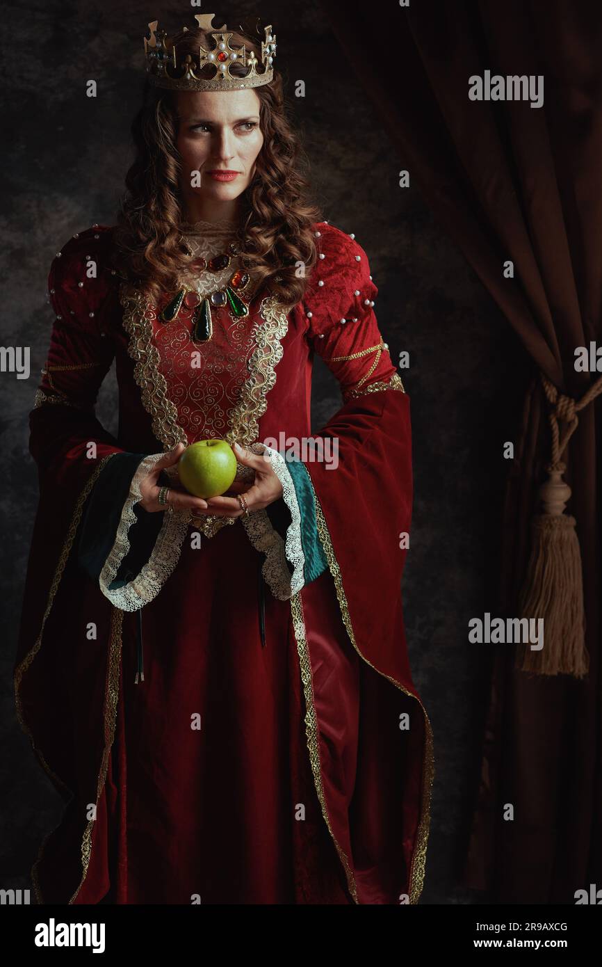 medieval queen in red dress with green apple and crown on dark gray ...