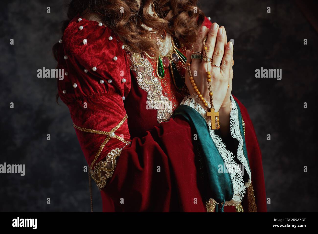 Closeup on medieval queen in red dress with rosary praying on dark gray ...