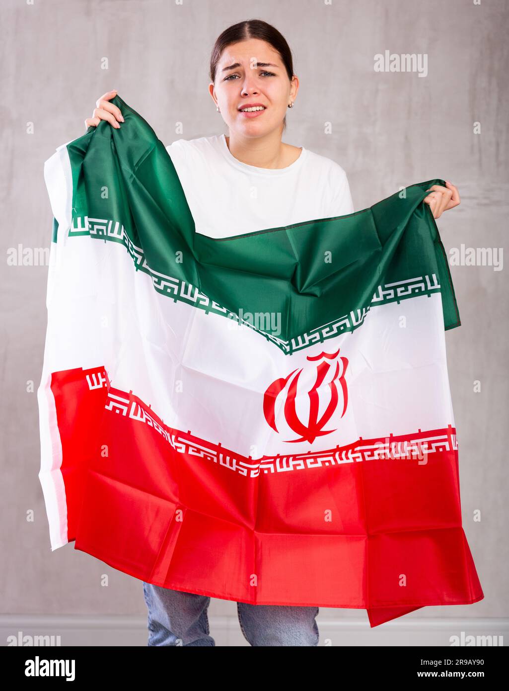 Sad young woman holding Iran flag against unicoloured background Stock ...