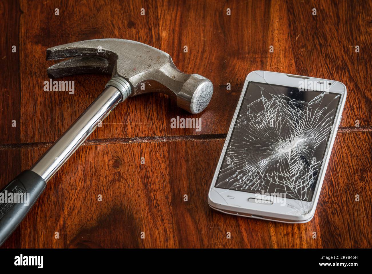 Smashed phone screen on a table with a hammer Stock Photo - Alamy
