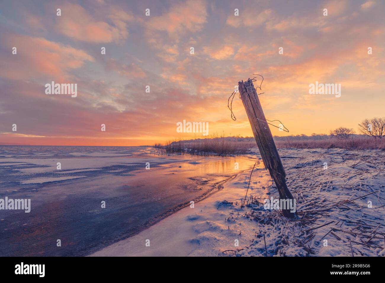 Fence post by a frozen lake in the sunrise Stock Photo - Alamy