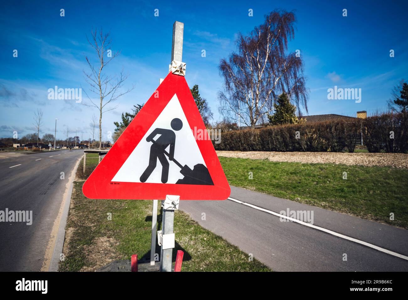 Road construction sign by a roadside in a city on a sunny day with blue ...