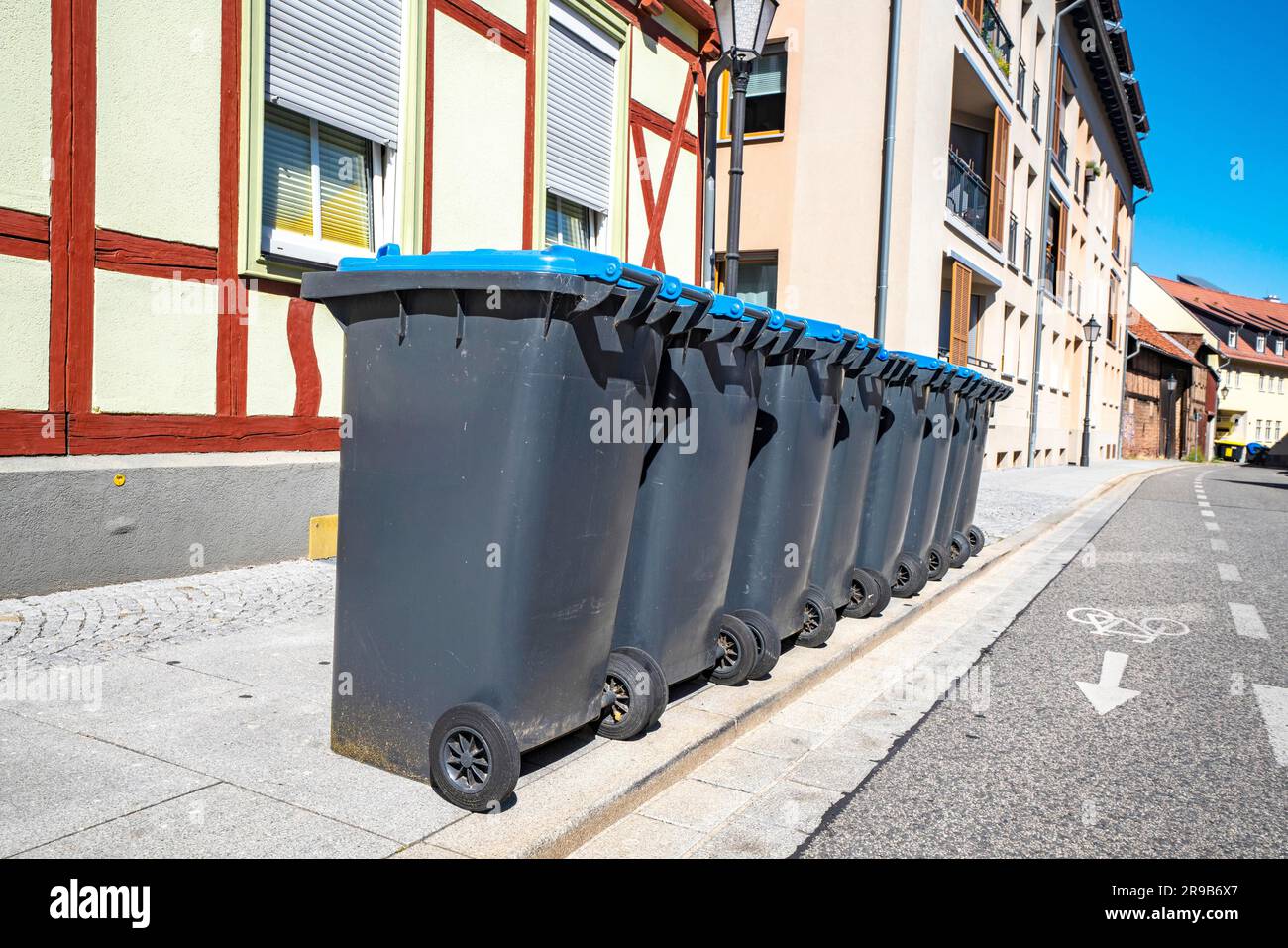 Eight garbage cans on the street outside an old house in the summer ...