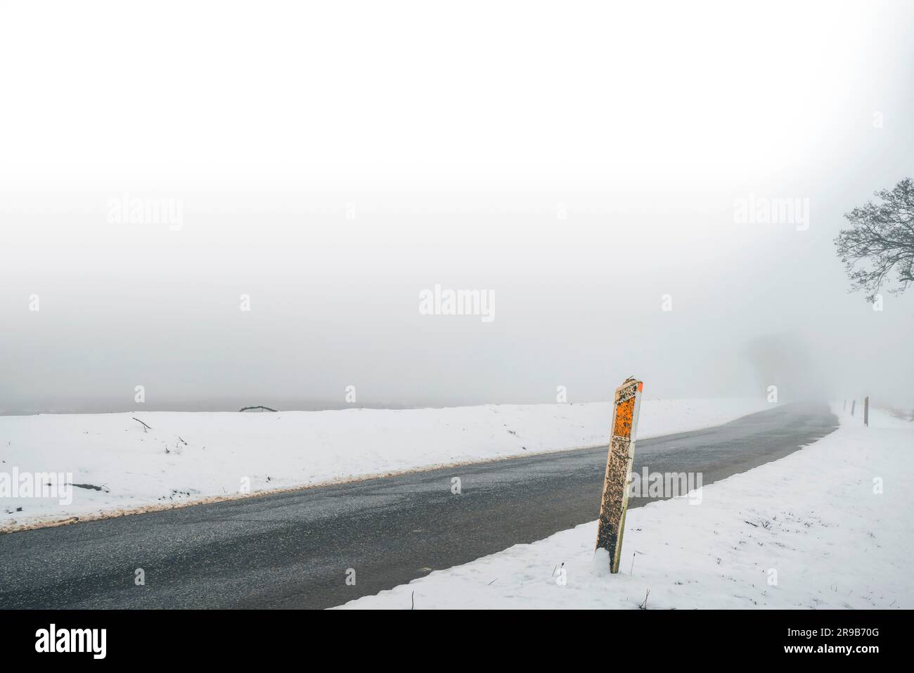 Marker post by a misty road in the winter with snow and a ice highway Stock Photo - Alamy