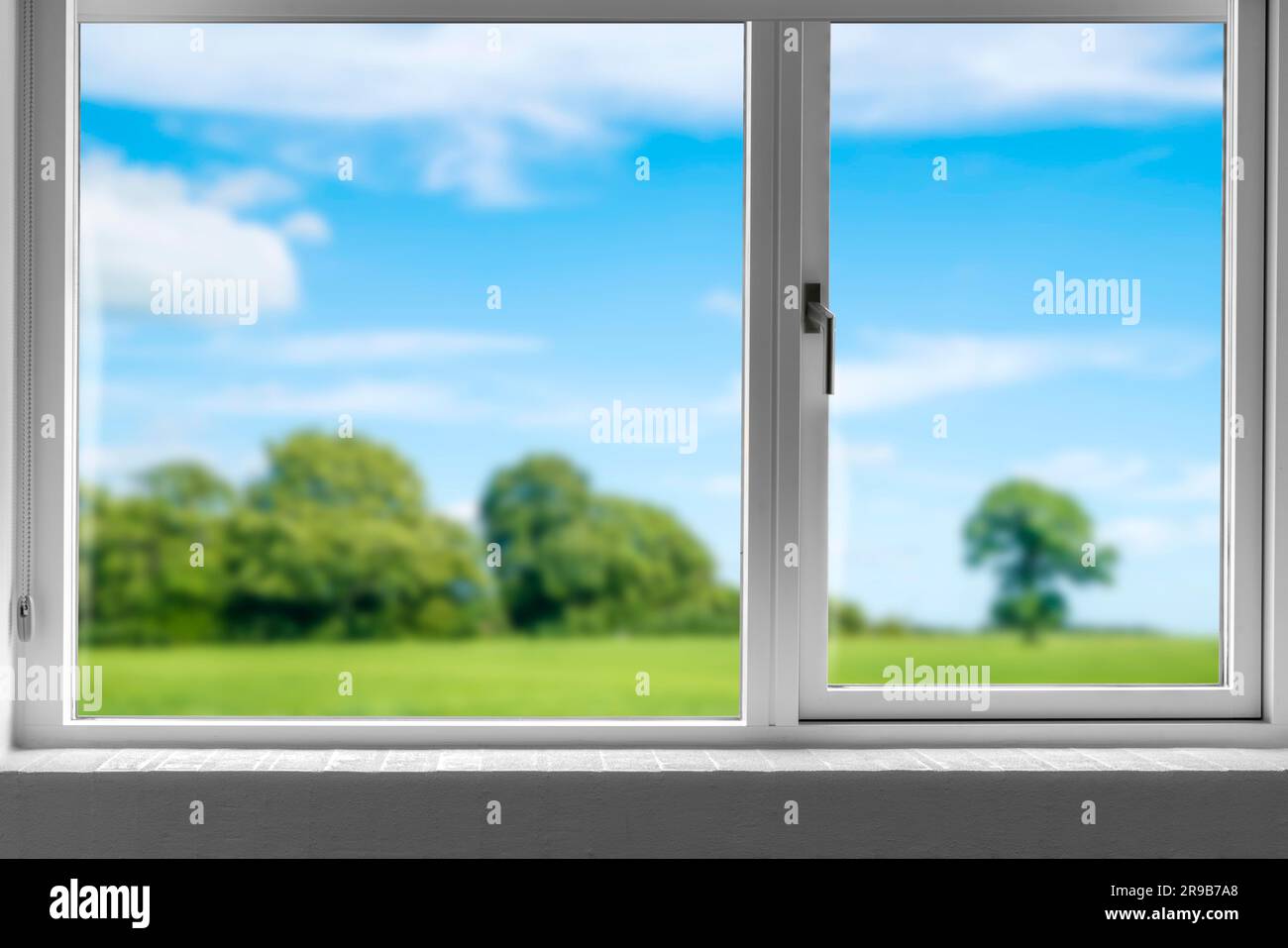 View from a closed window to a green meadow with trees under a blue sky ...