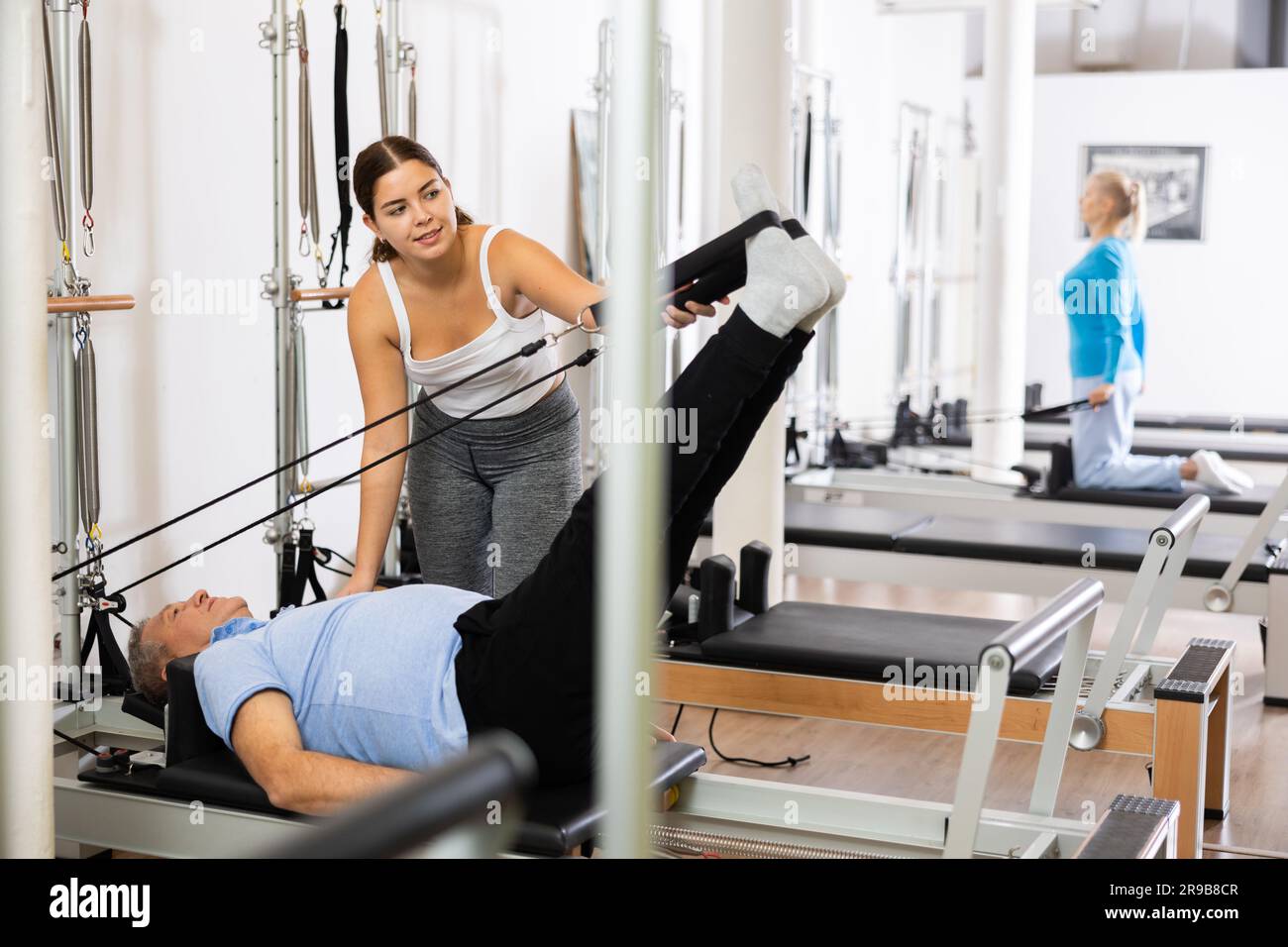Sporty young woman coach controlling movements of elderly man training ...