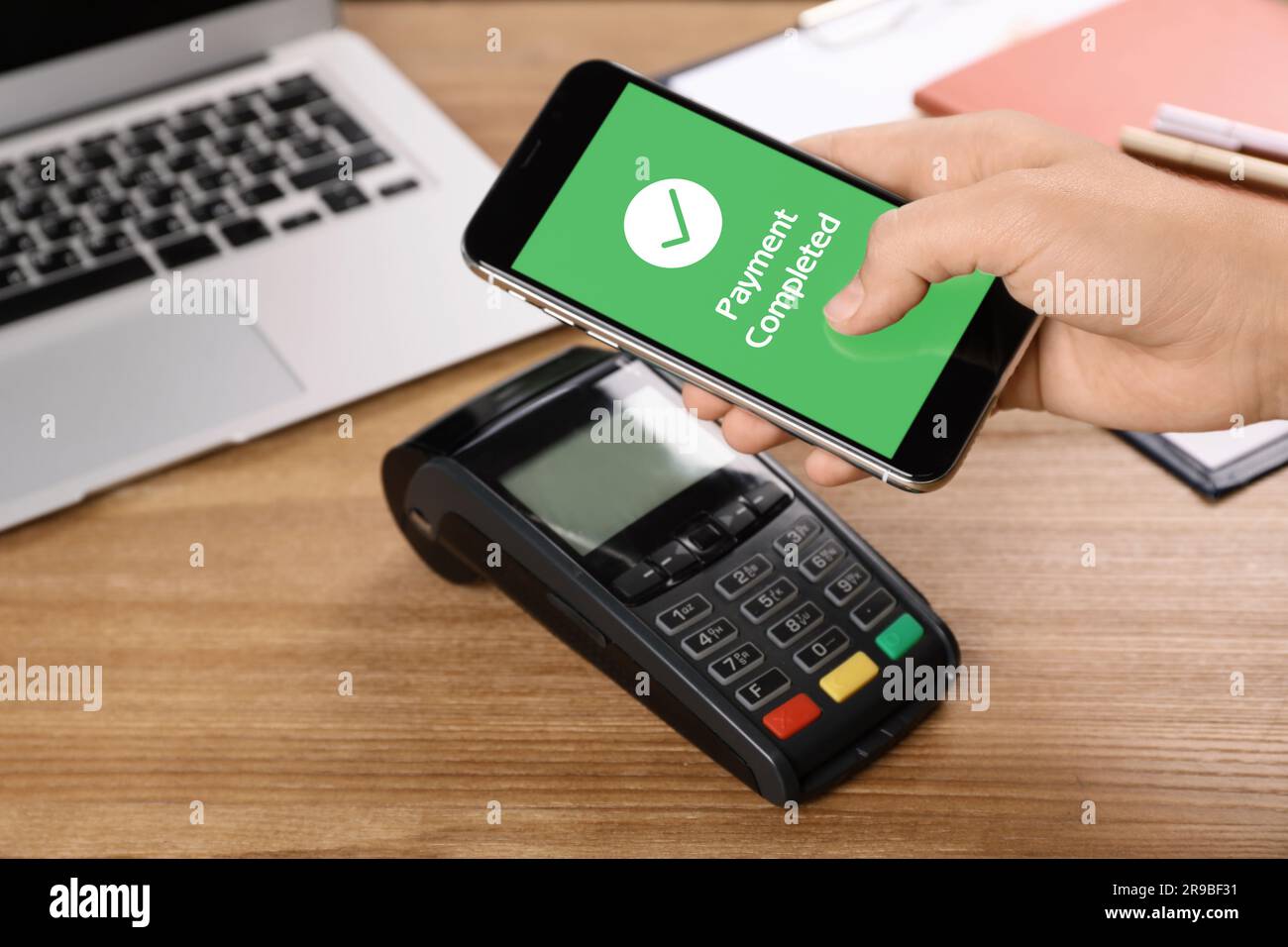 Woman using terminal for contactless payment with smartphone at wooden ...