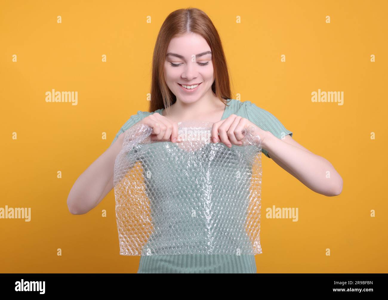 Woman popping bubble wrap on yellow background. Stress relief Stock ...