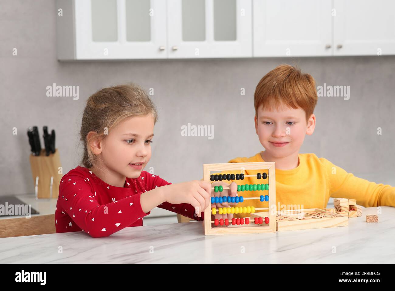 Happy children playing with abacus at white marble table in kitchen ...