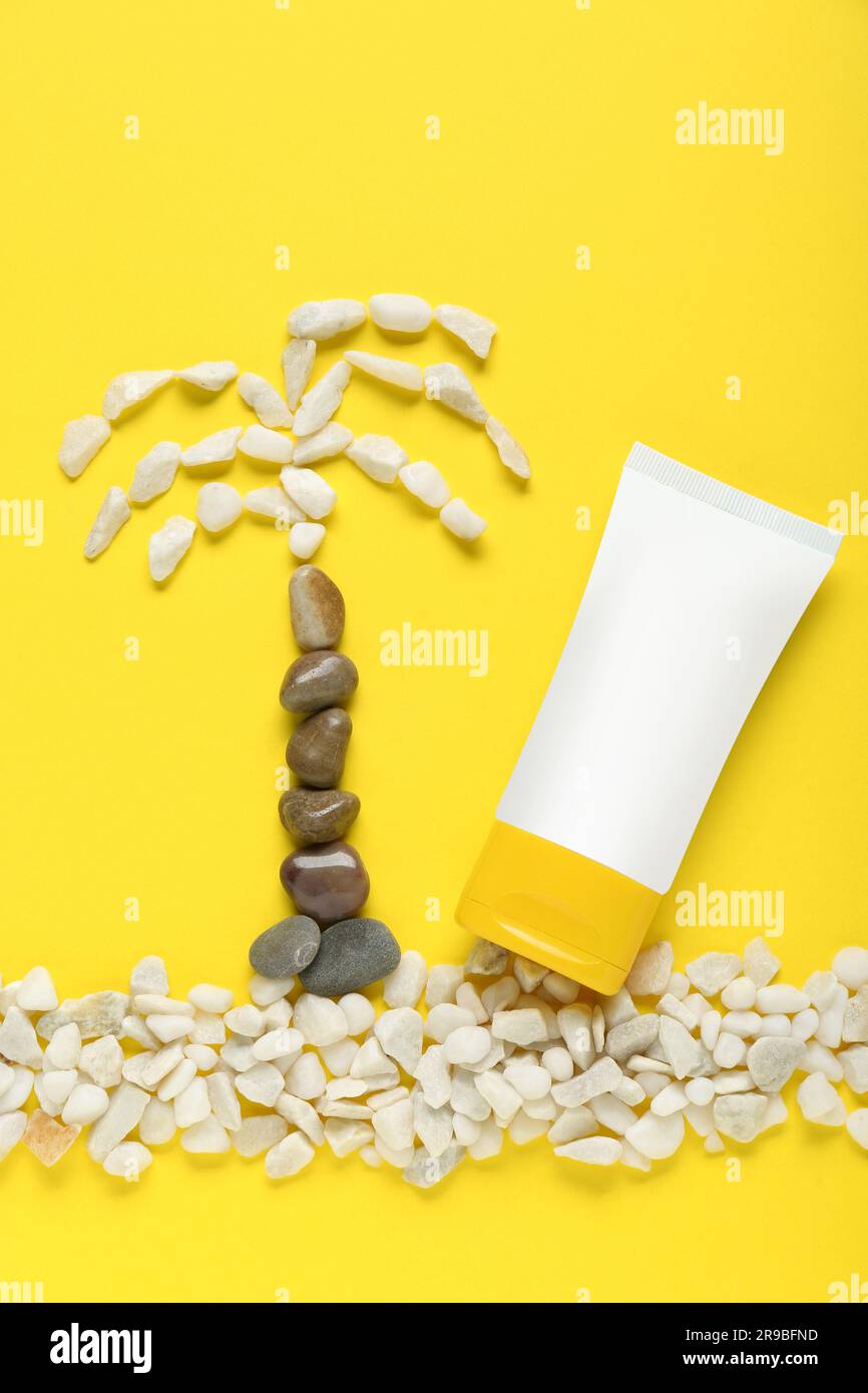 Suntan cream and palm made of marble pebbles on yellow background, flat ...