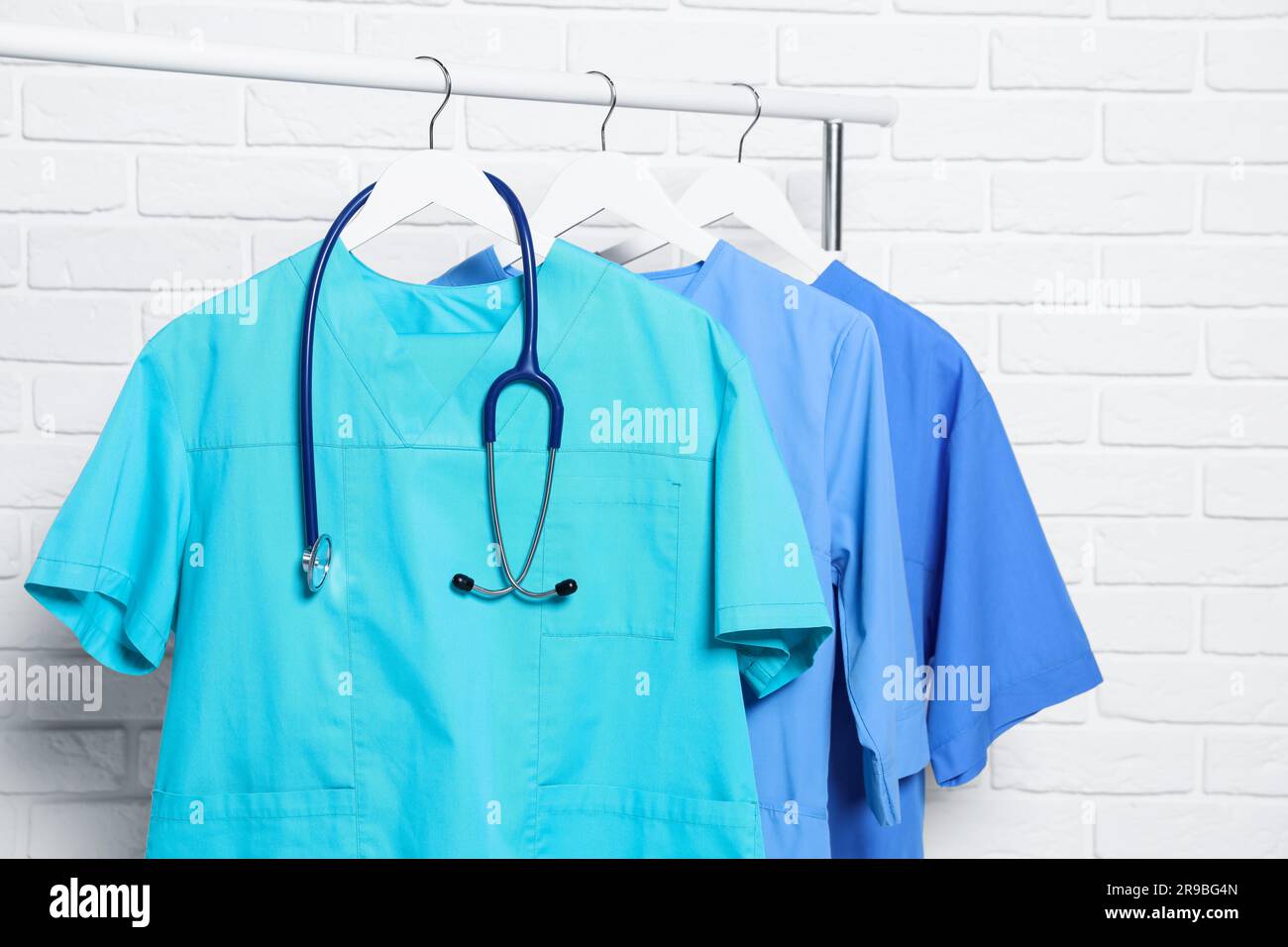 Medical uniforms and stethoscope hanging on rack near white brick wall ...