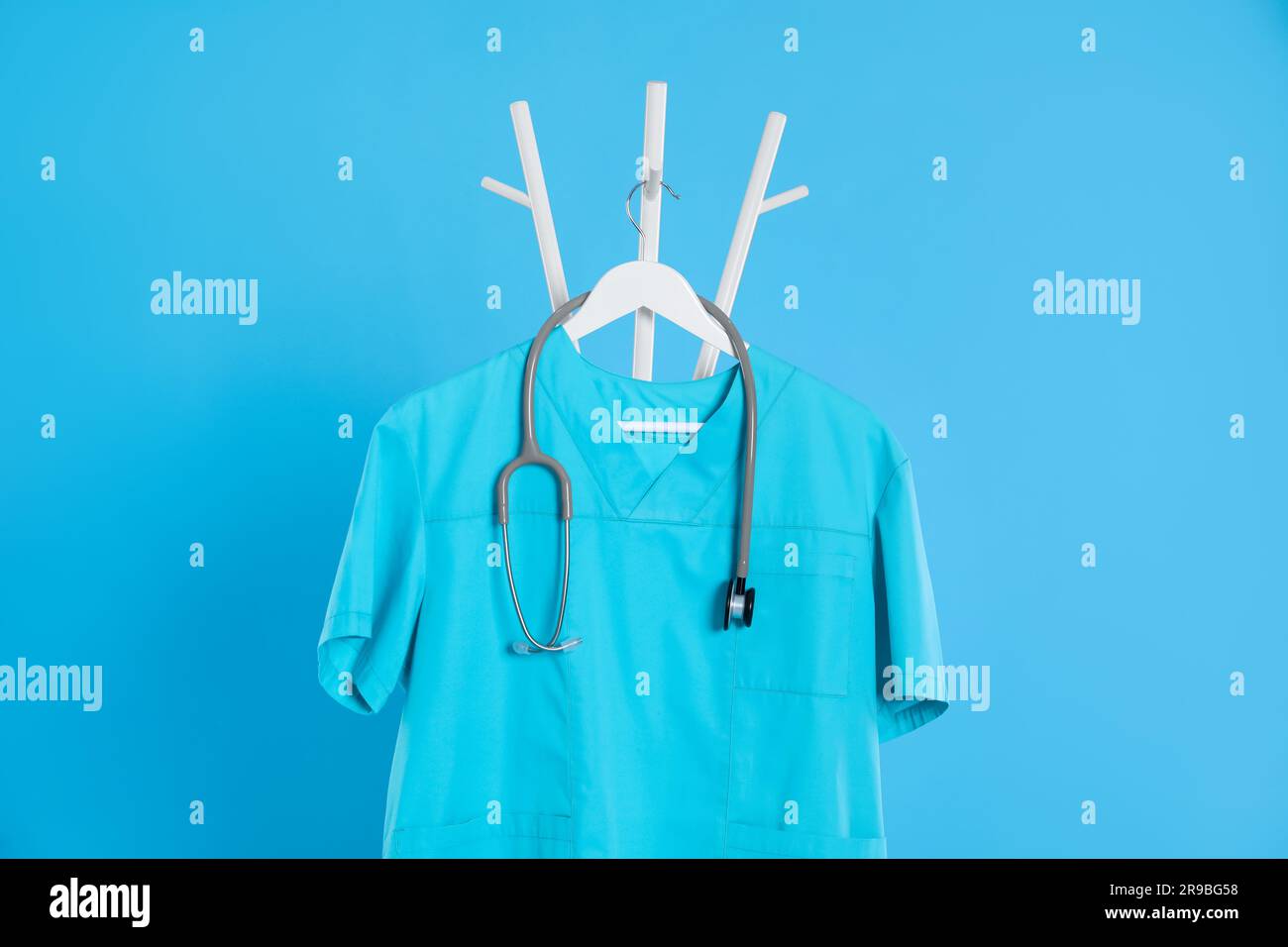 Turquoise medical uniform and stethoscope hanging on rack against light ...