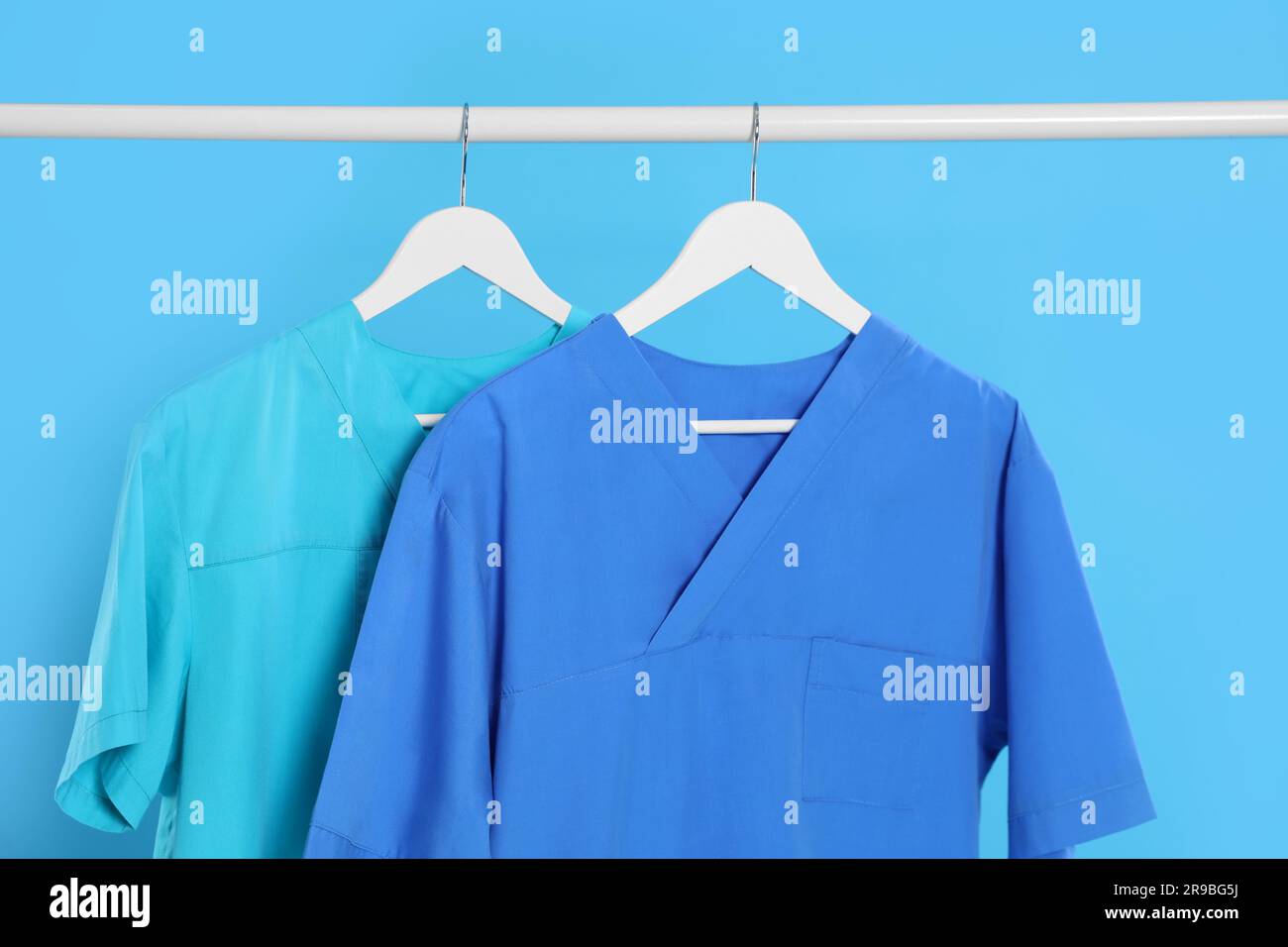 Medical uniforms on rack against light blue background Stock Photo - Alamy