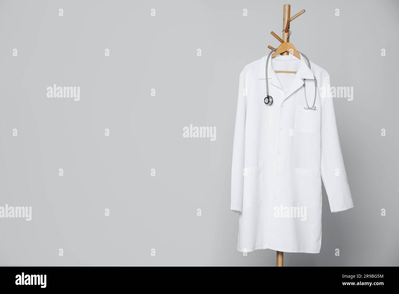 Medical uniform and stethoscope hanging on rack against light grey ...