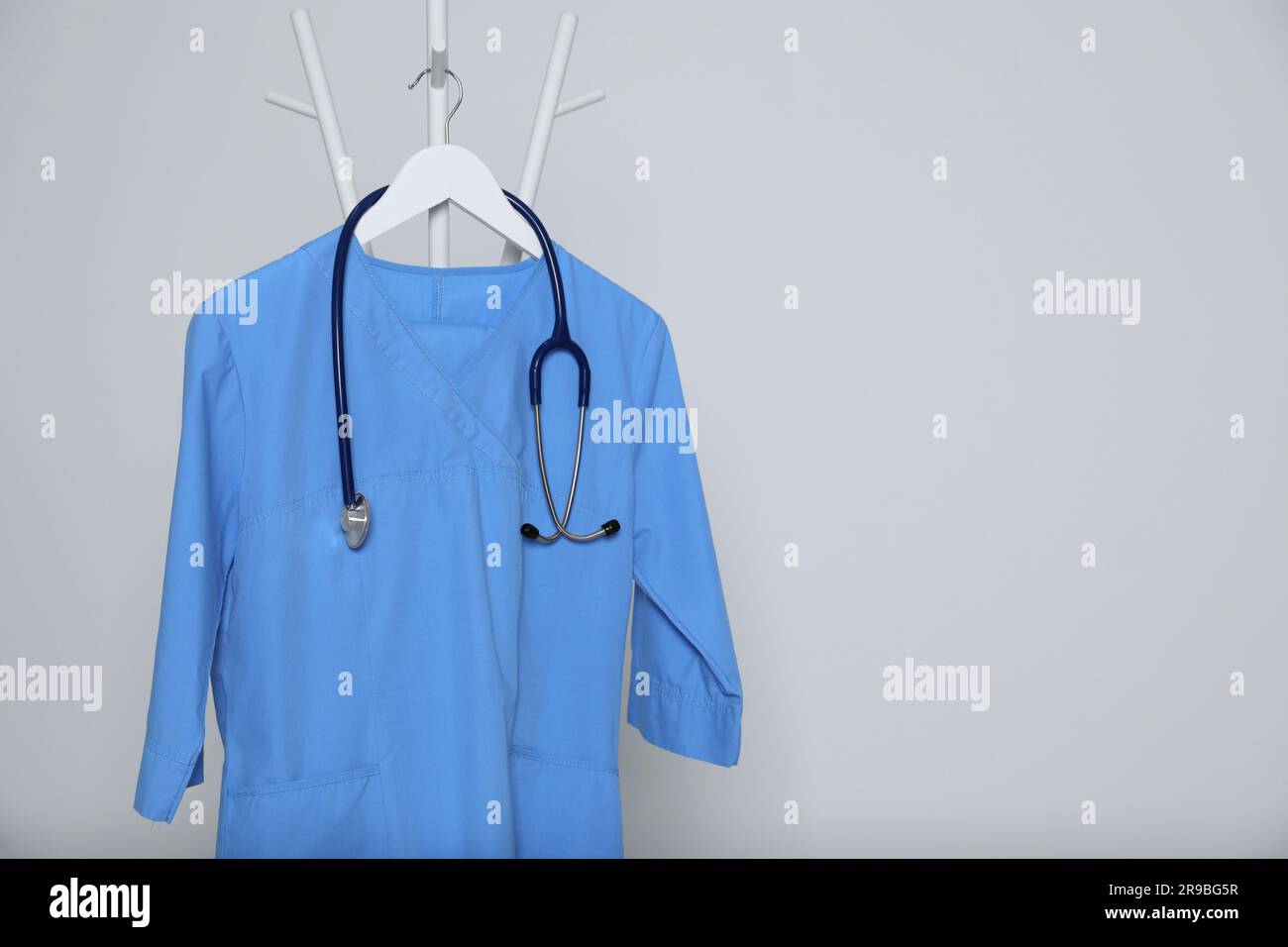 Medical uniform and stethoscope hanging on rack against light grey ...