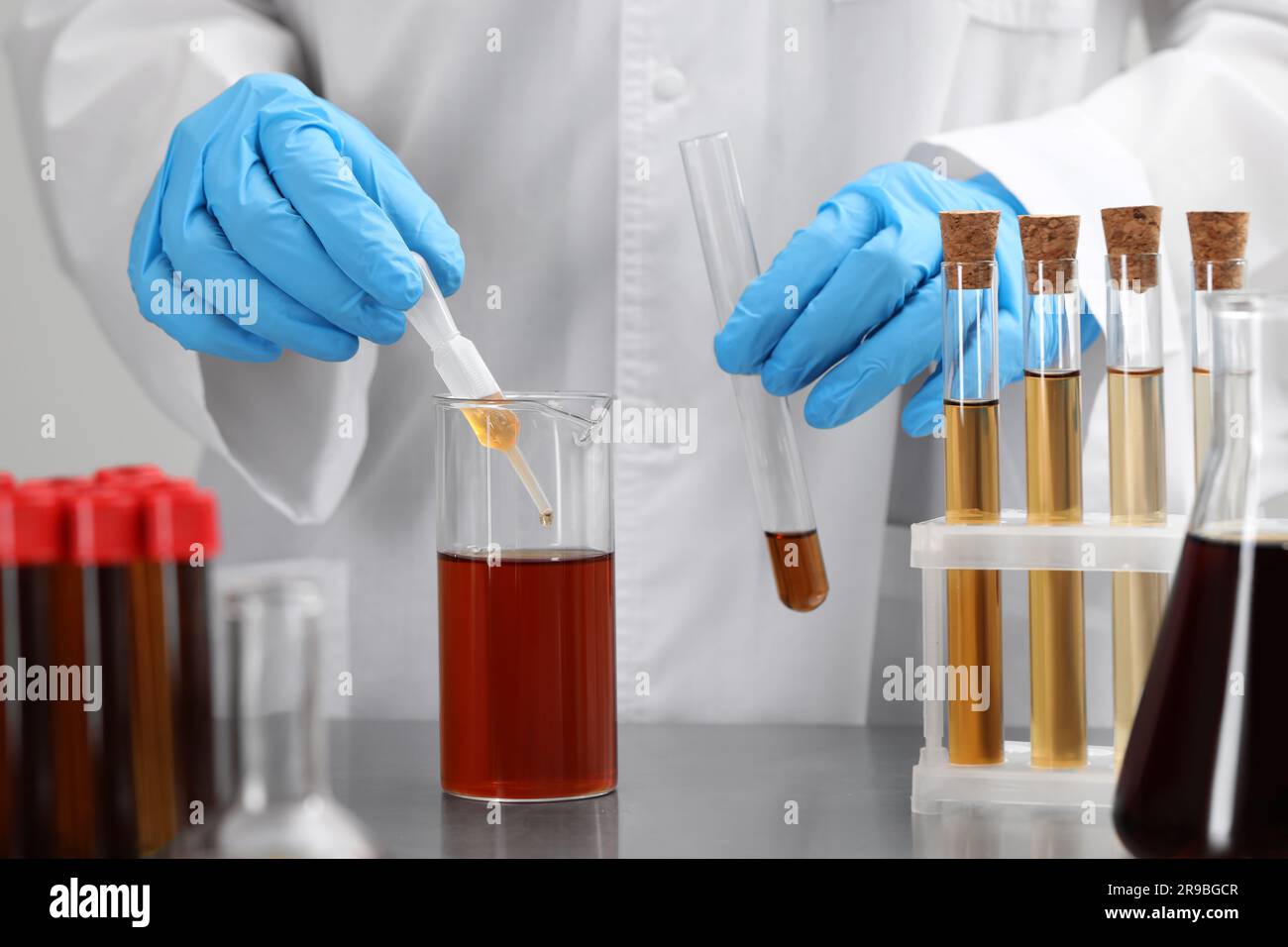 Scientist dripping brown liquid from pipette into beaker at table ...
