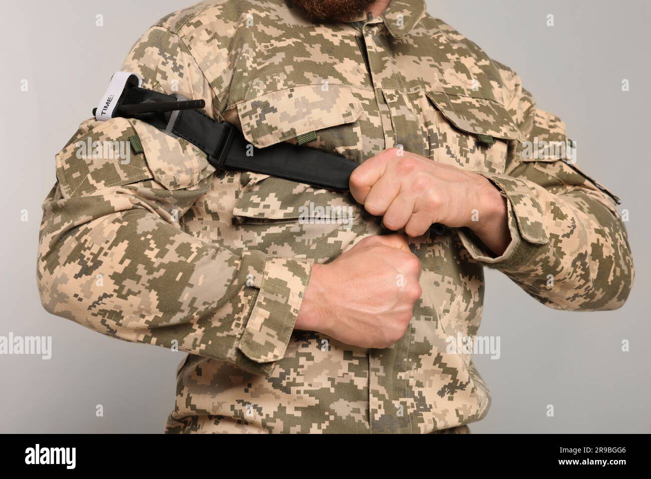 Soldier in military uniform applying medical tourniquet on arm against ...
