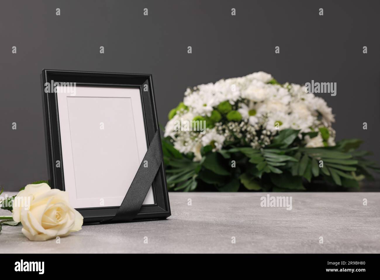 Photo frame with black ribbon, rose on light table and wreath of ...