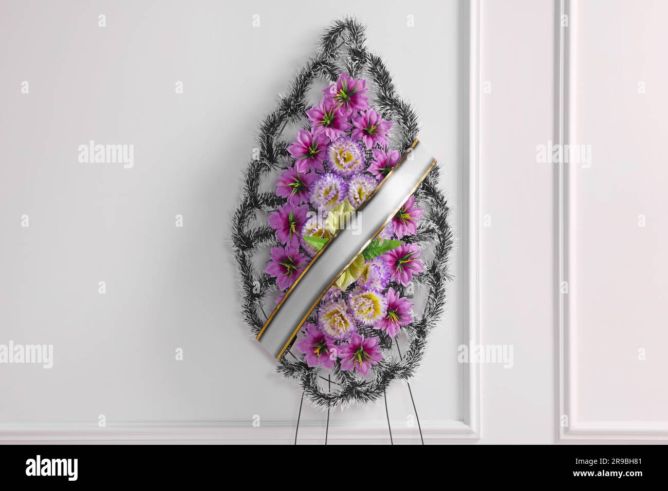 Funeral wreath of plastic flowers with ribbon near white wall Stock ...