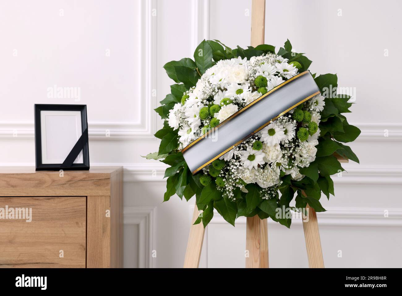 Wreath of flowers and photo frame with black ribbon on commode in room ...