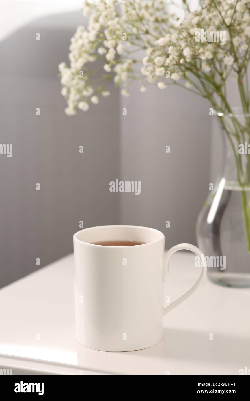 Ceramic mug with tea on white bedside table indoors. Mockup for design ...