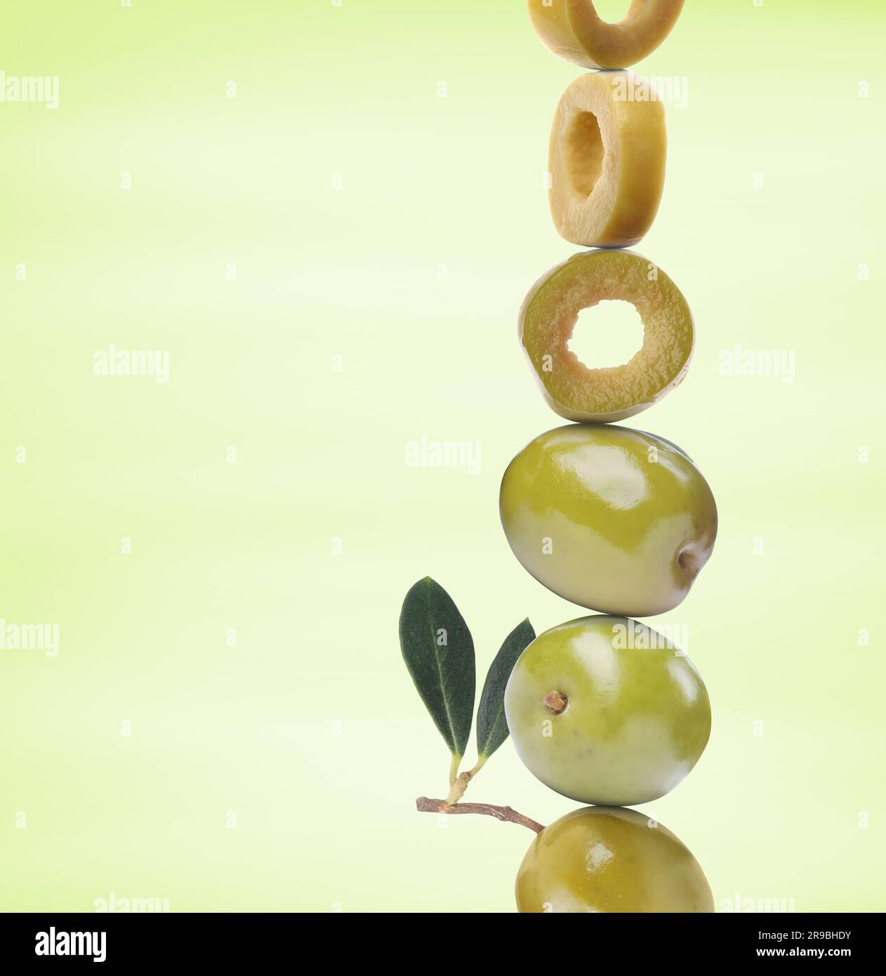 Cut and whole olives with leaves on yellowish green gradient background ...