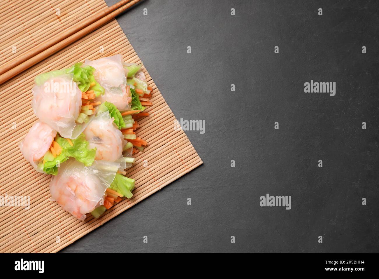 Tasty spring rolls, chopsticks and bamboo mat on grey textured table ...