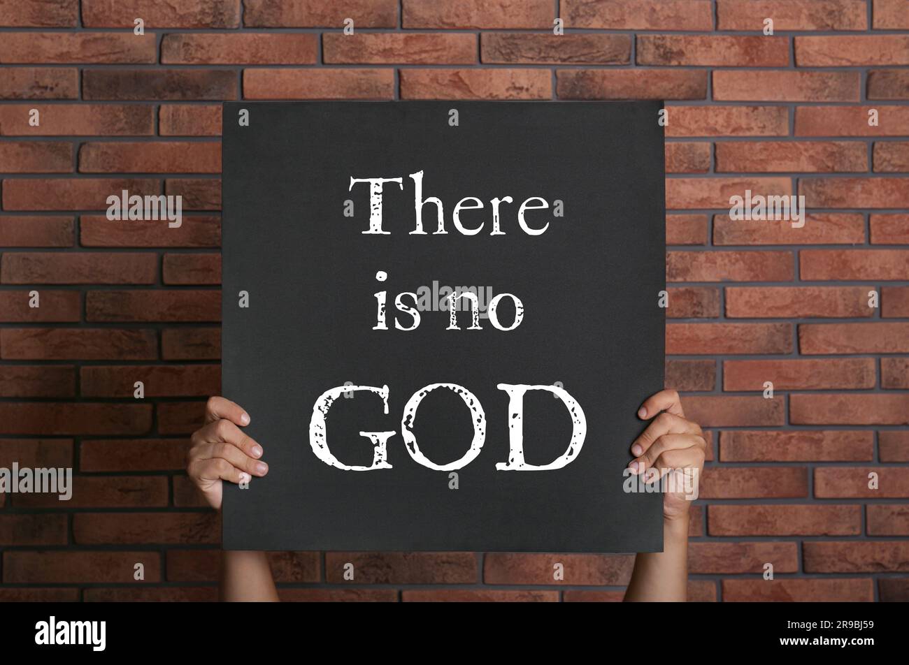 Atheism. Man holding sign with text There Is No God near brick wall ...