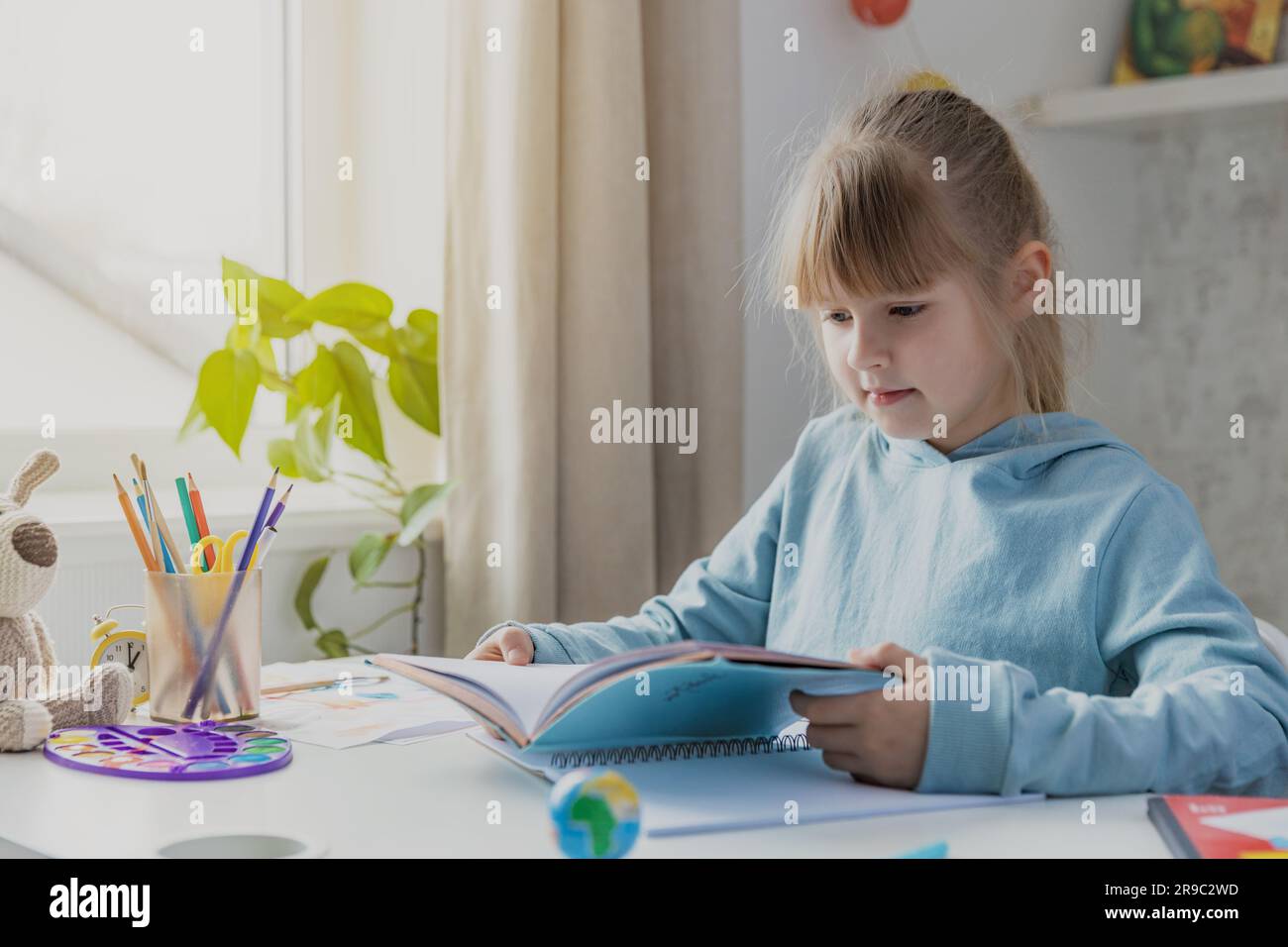 Schooler cute little girl sitting at desk in bedroom, holding a book ...