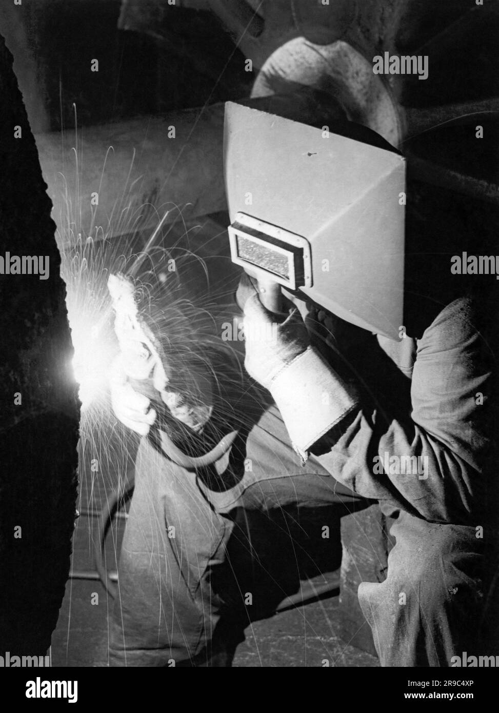 United States: c. 1936 A welder using an arc welder and holding his ...