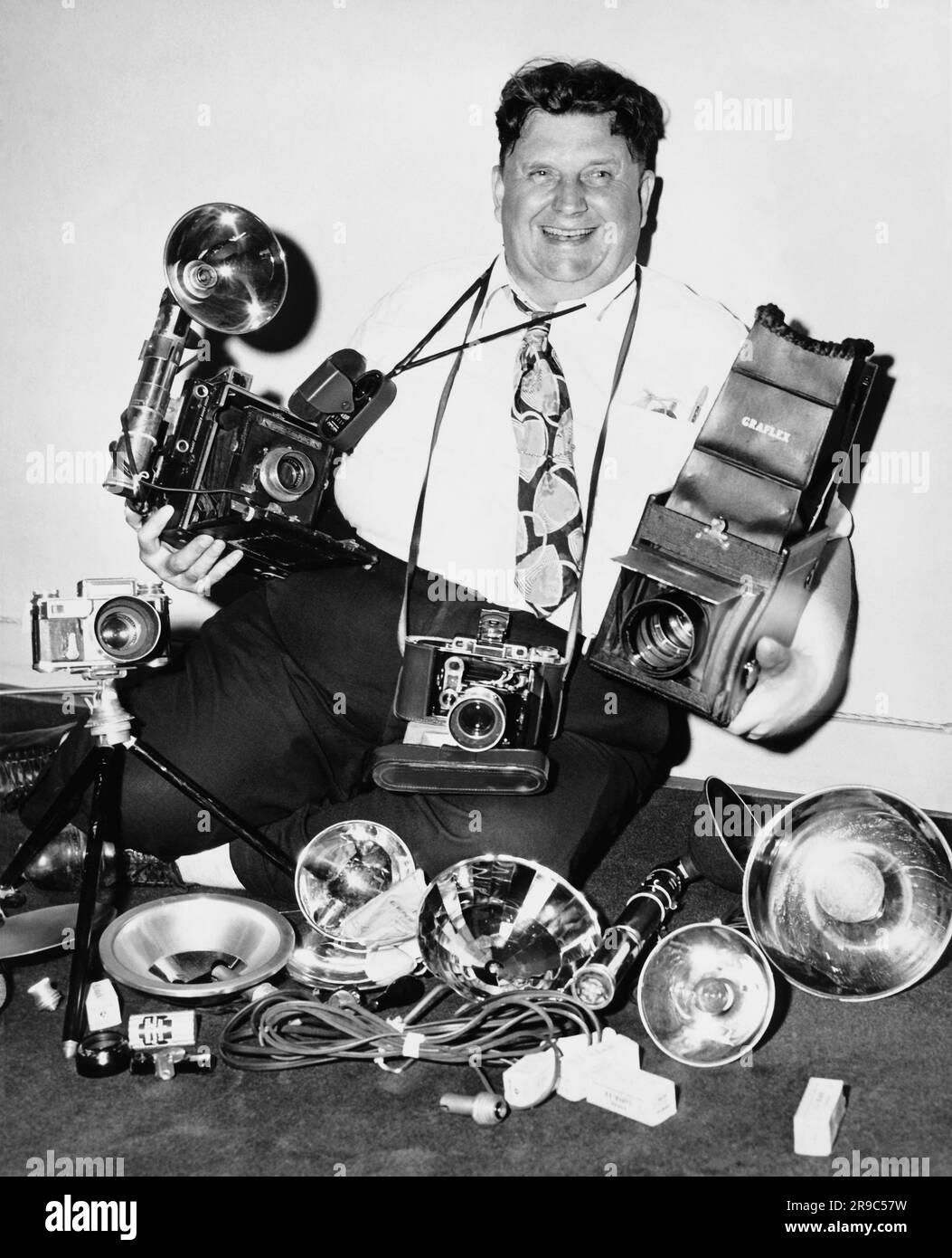 United States: c. 1954 A smiling press photographer surrounded by his ...