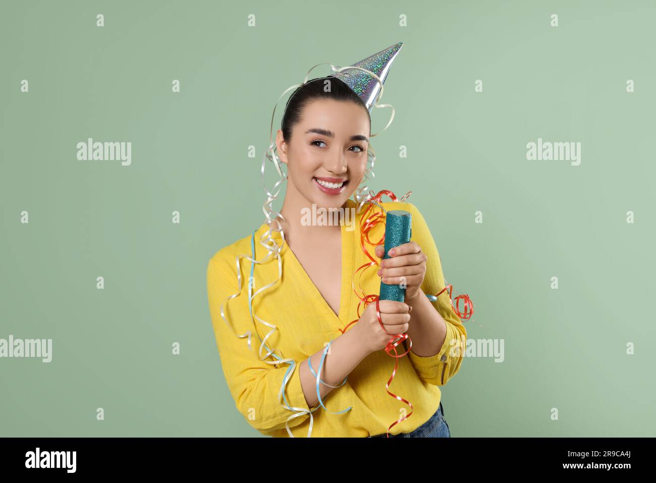 Young woman blowing up party popper on pale green background Stock ...