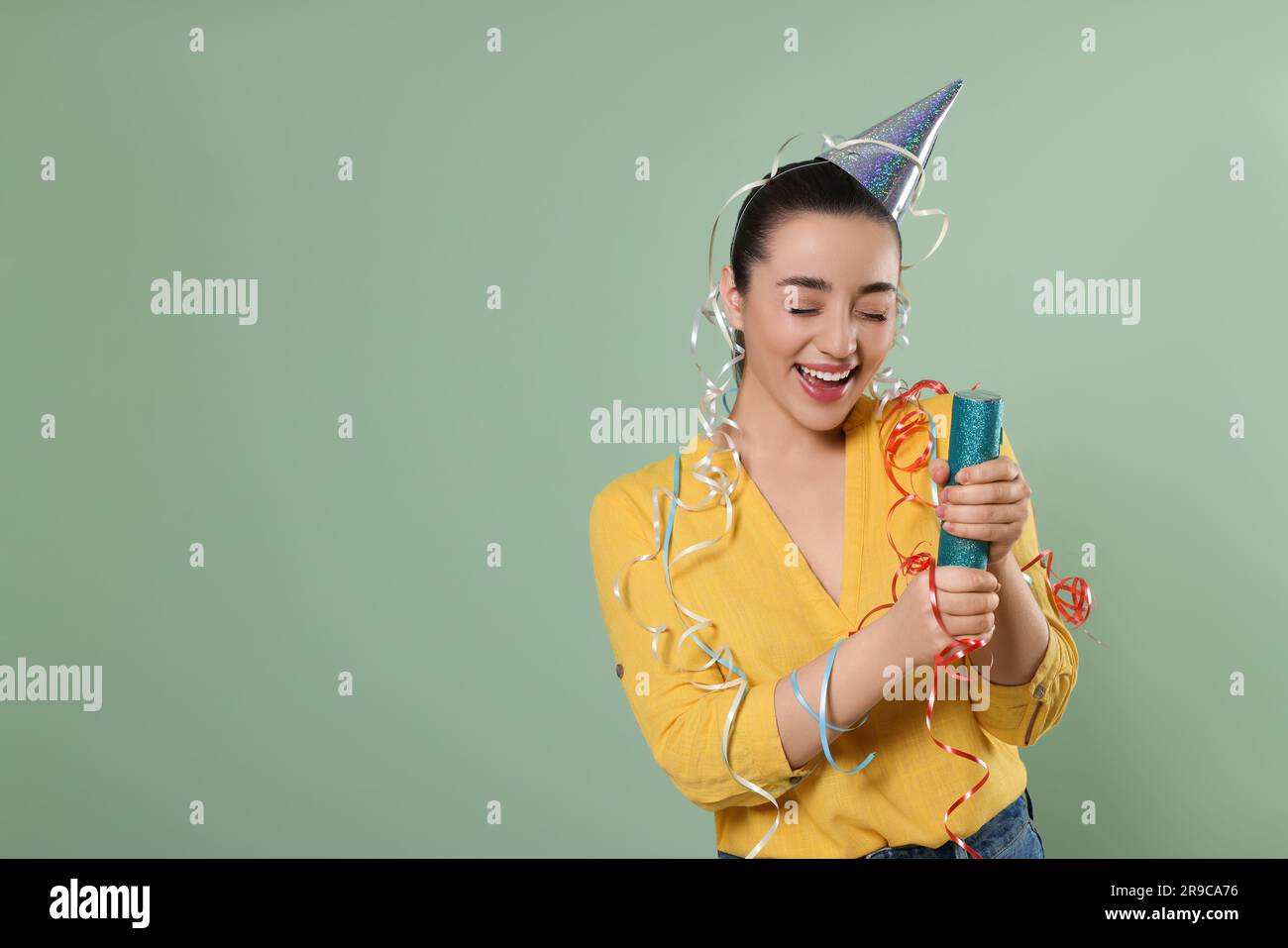 Young woman blowing up party popper on pale green background, space for ...