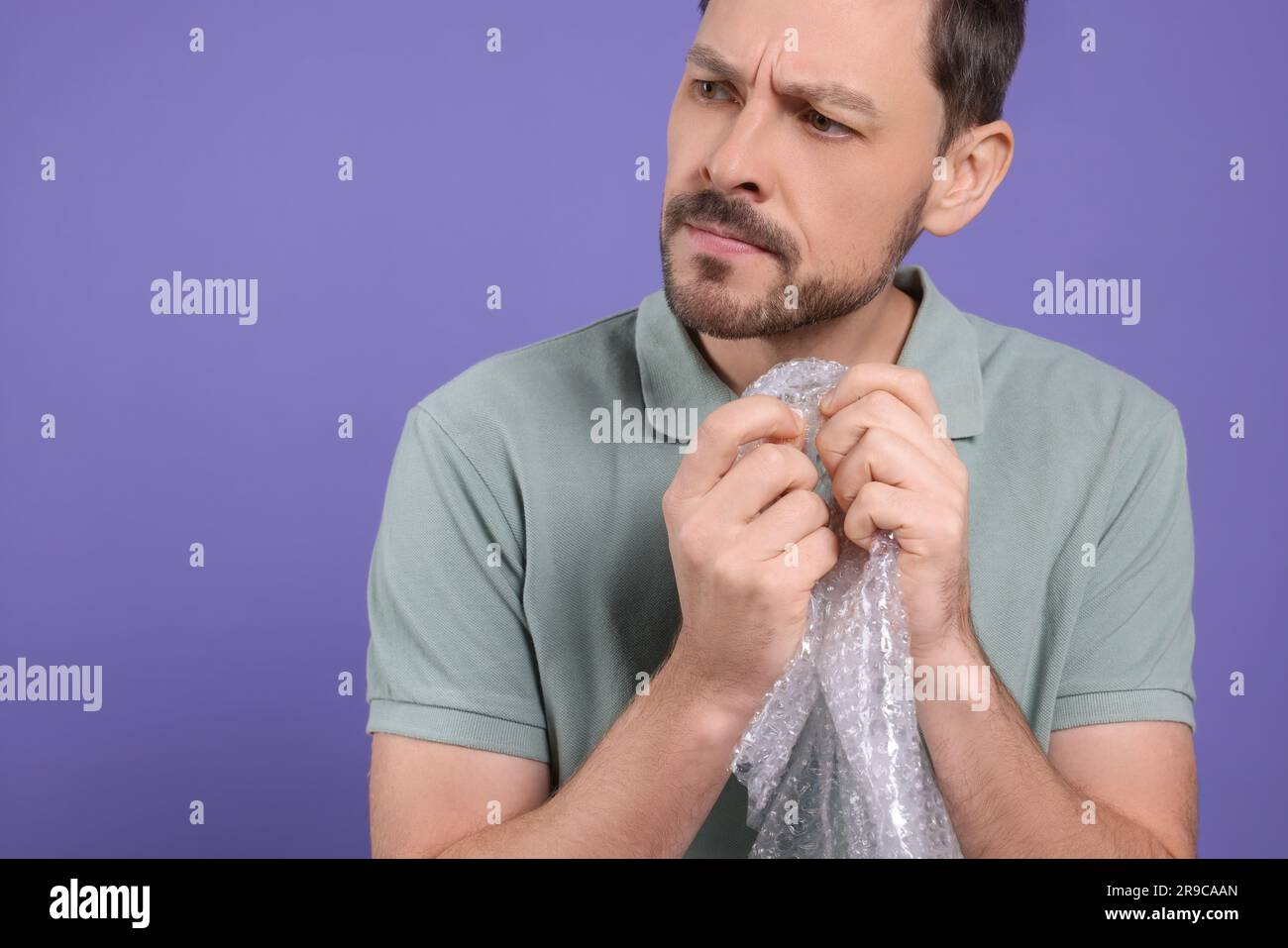 Angry man popping bubble wrap on purple background, closeup. Space for ...