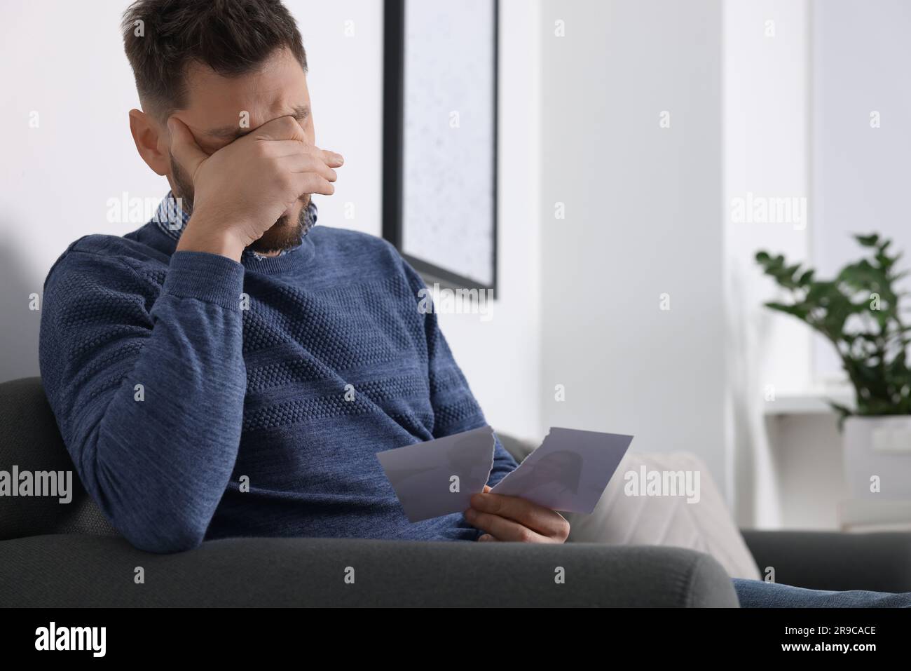 Crying man holding torn photo on sofa indoors. Divorce concept Stock ...