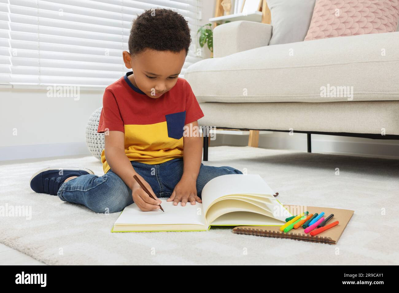 Cute African-American boy drawing in sketchbook with colorful markers ...