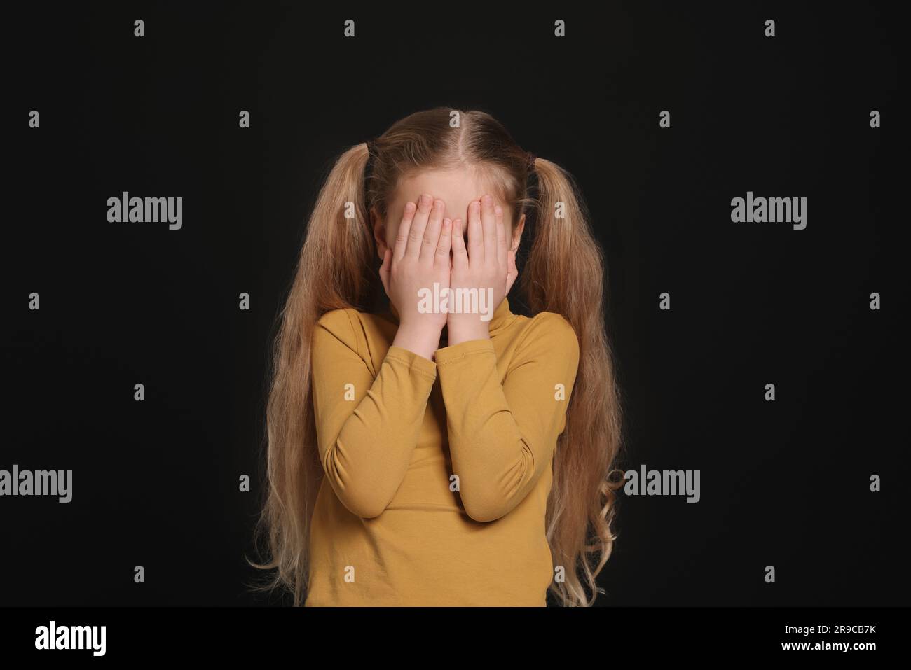 Girl covering face with hands on black background. Children's bullying ...