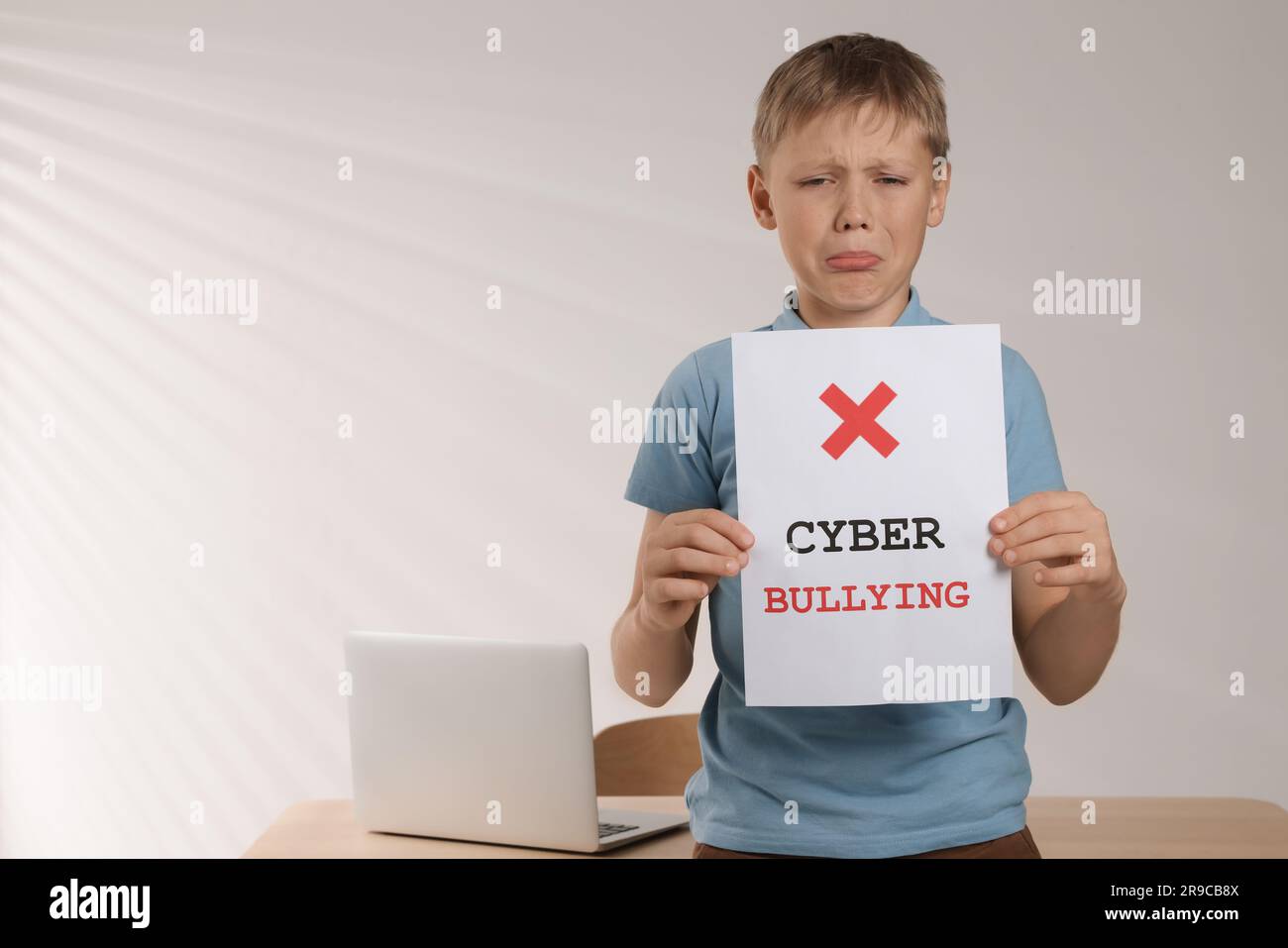Upset holding sign with phrase Cyber Bullying near table indoors, space ...