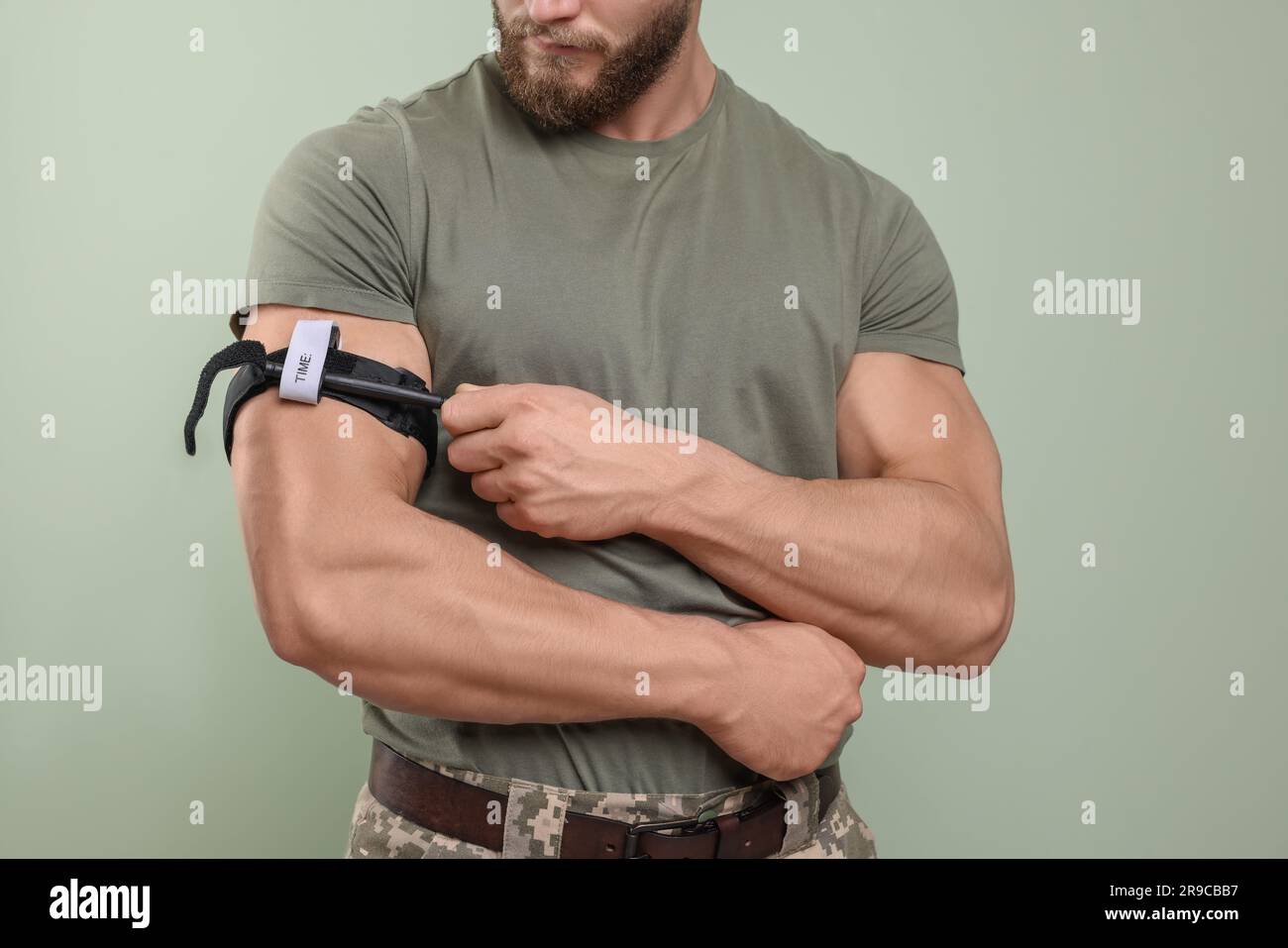 Soldier in military uniform applying medical tourniquet on arm against ...