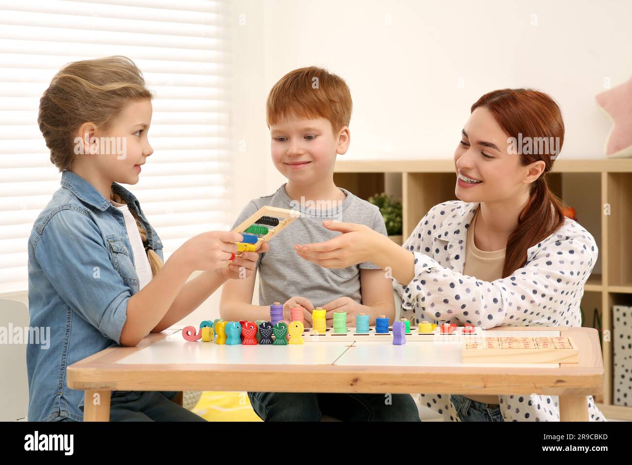 Happy mother and children playing with different math game kits at desk ...