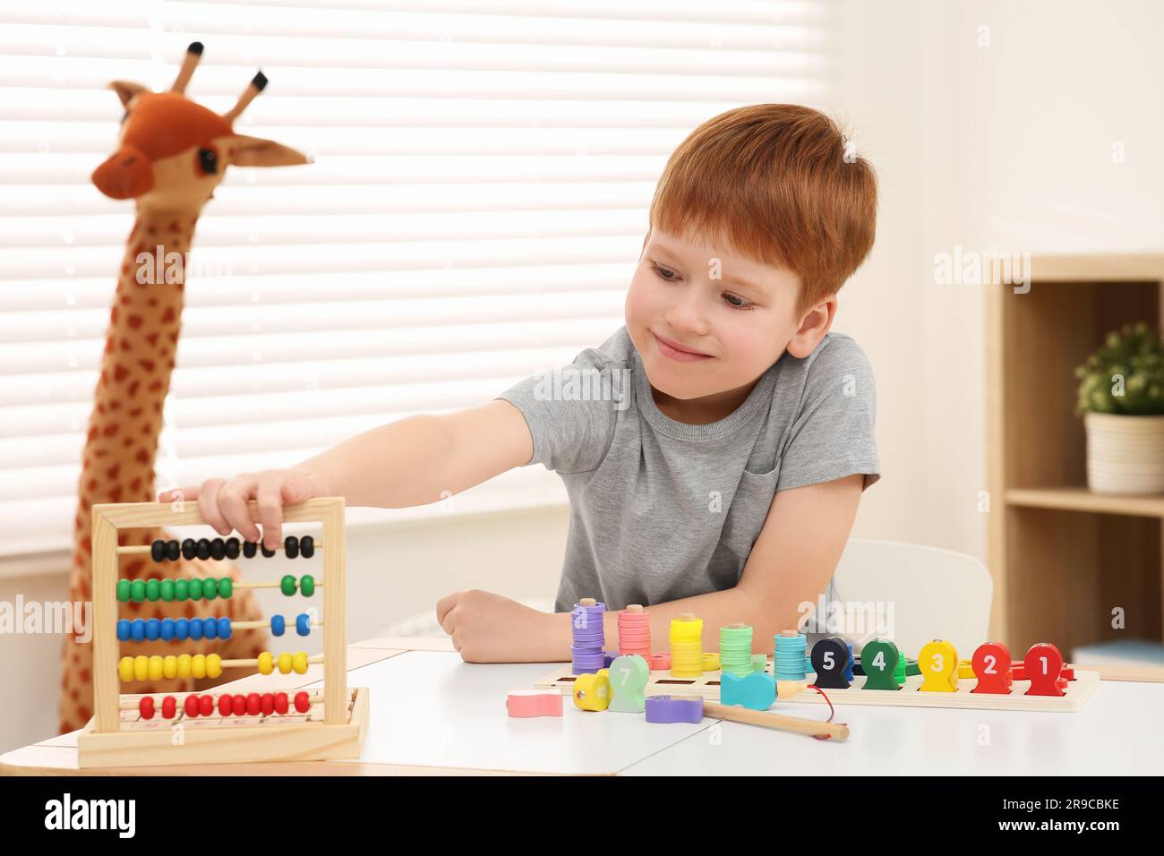 Happy little boy playing with abacus at desk in room. Learning ...