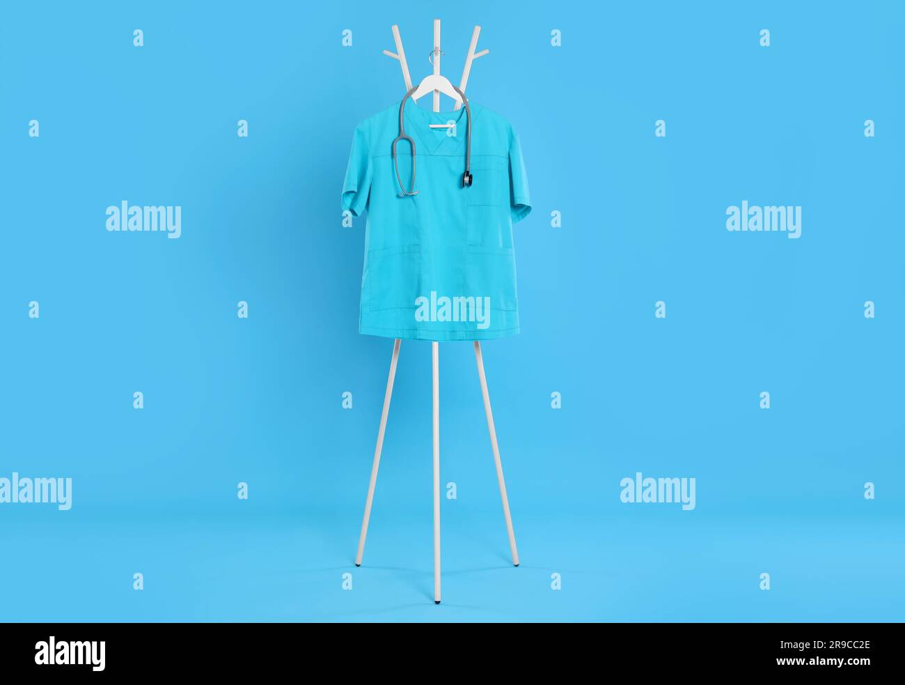 Turquoise medical uniform and stethoscope hanging on rack against light ...