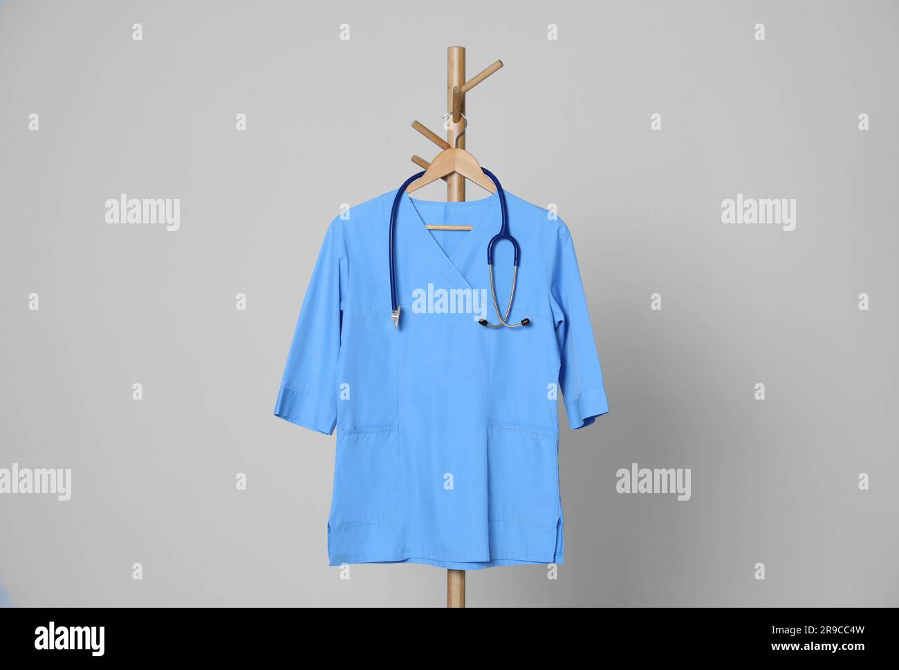 Medical uniform and stethoscope hanging on rack against light grey ...