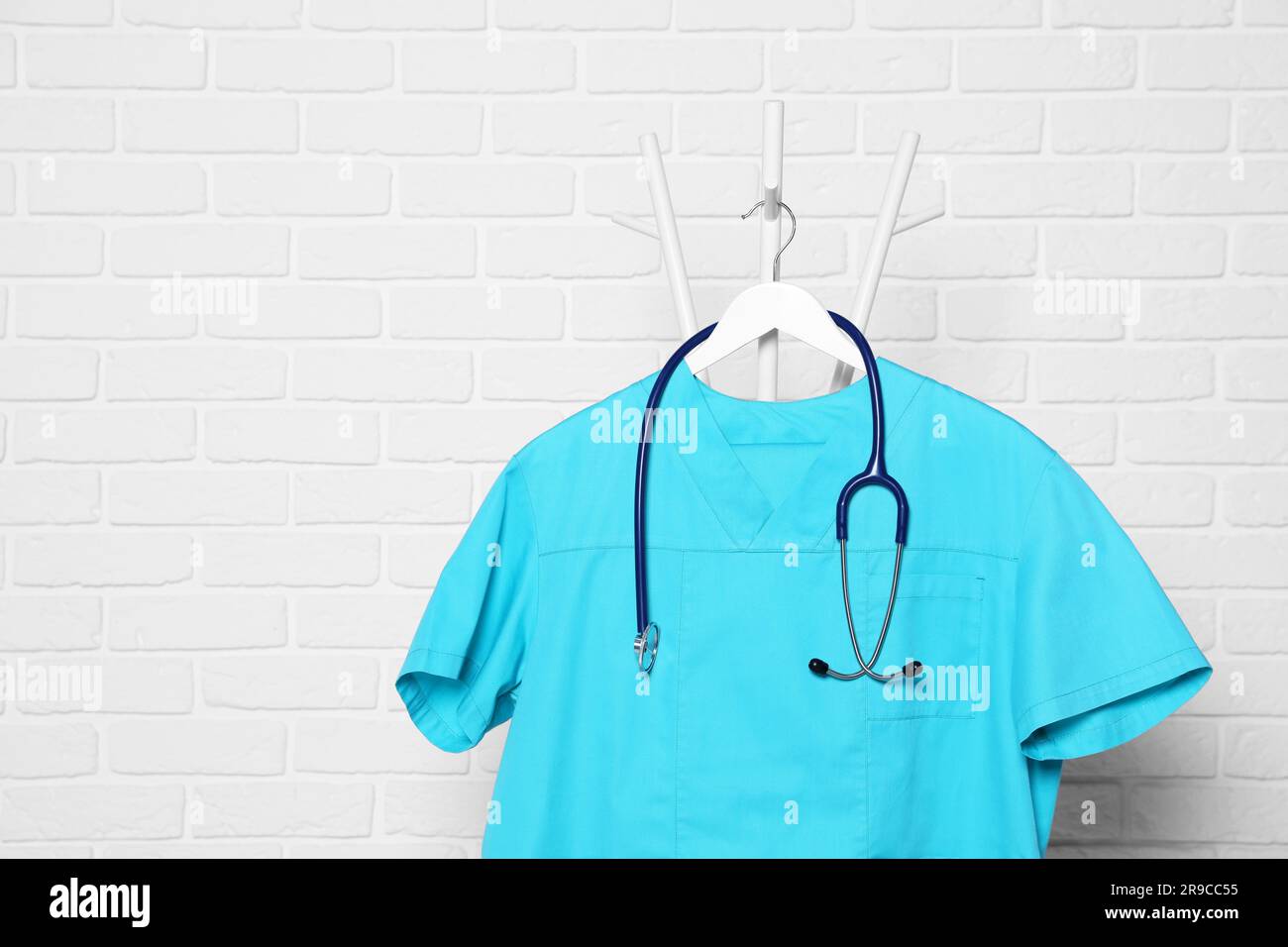 Turquoise medical uniform and stethoscope hanging on rack near white ...