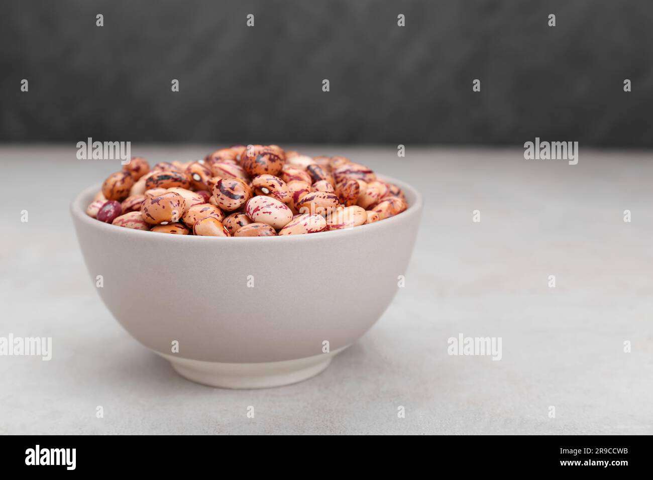 Bowl with dry kidney beans on light grey table, closeup. Space for text ...