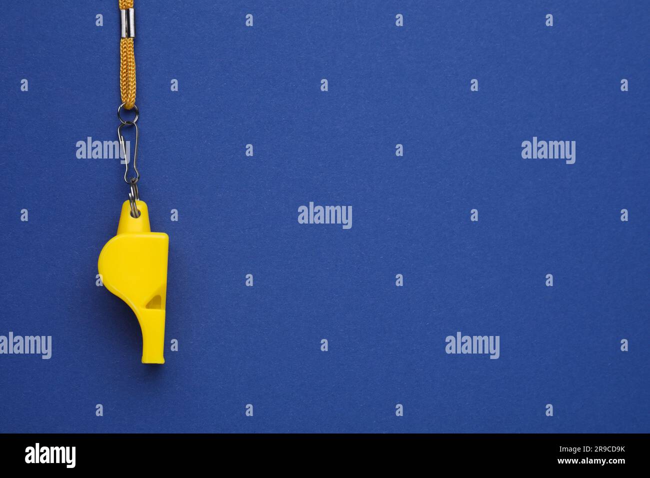One yellow whistle with cord on blue background, top view. Space for ...