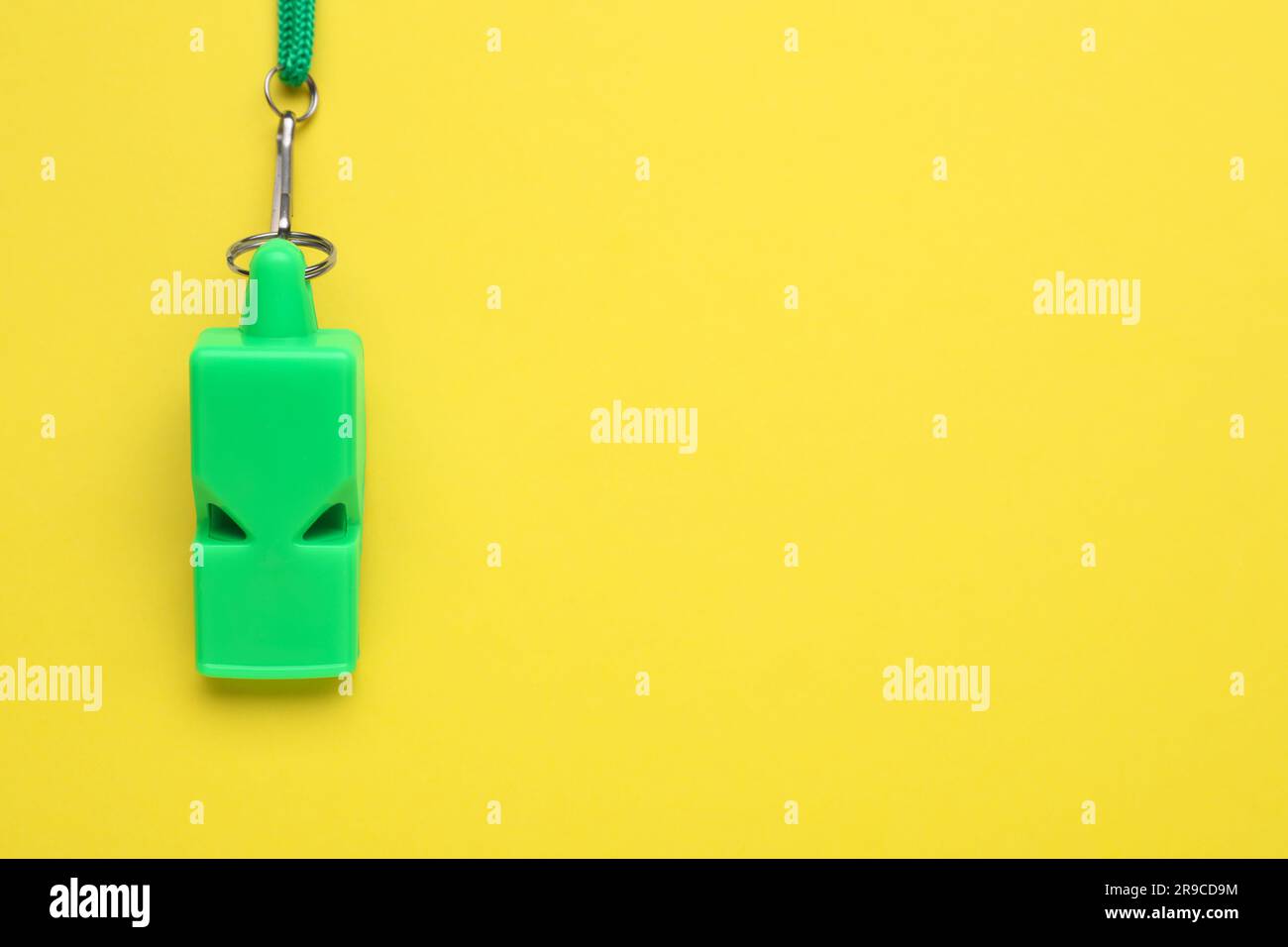 One green whistle with cord on yellow background, top view. Space for ...